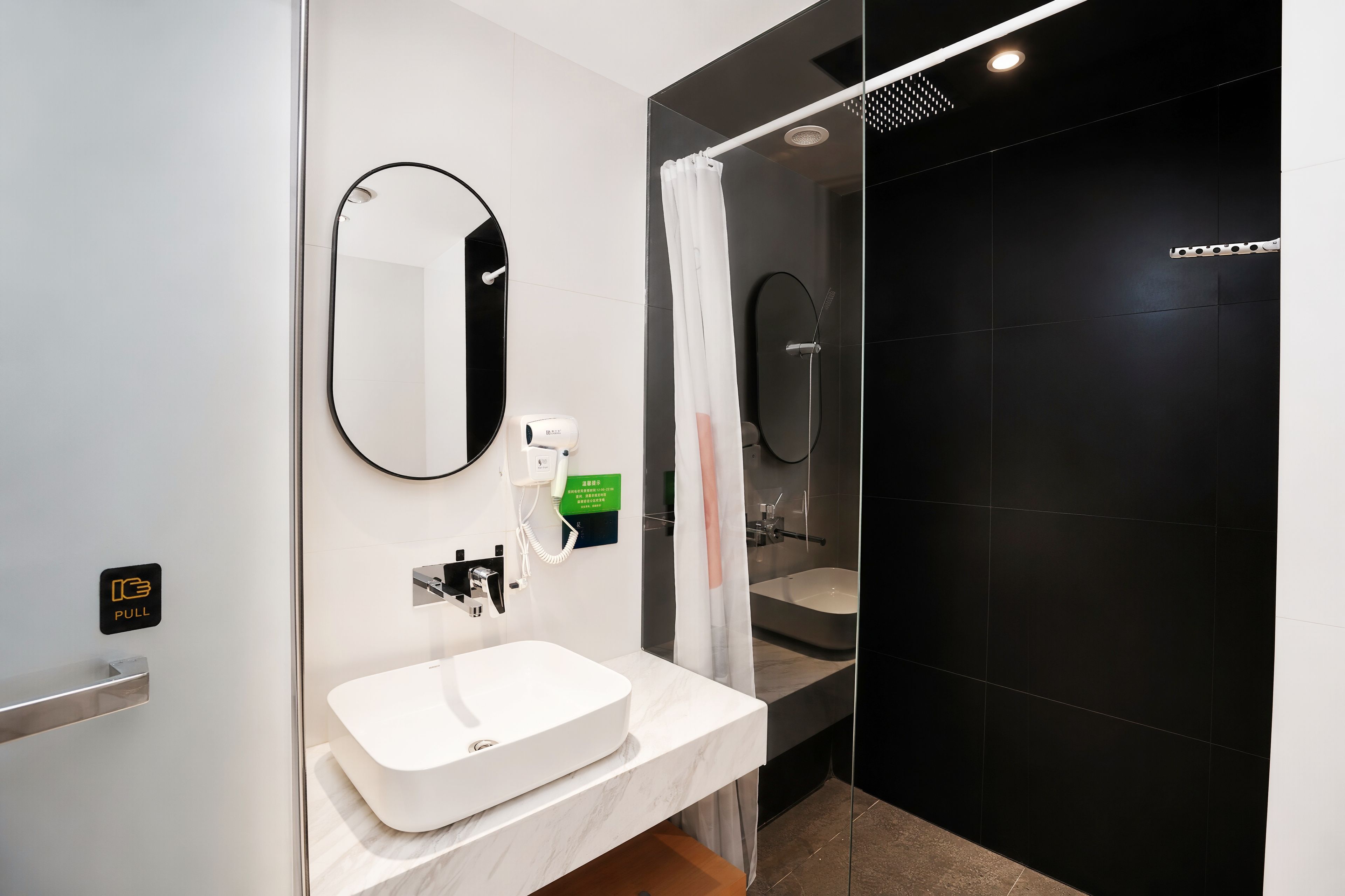 Casa de banho moderna com lavatório branco, espelho, chuveiro com porta de vidro e parede preta.