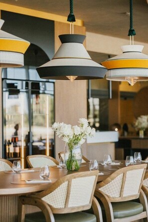 Uma sala de jantar com uma mesa redonda posta para quatro pessoas, rodeada por cadeiras de vime com almofadas verdes.