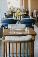Ambiente de restaurante com mesas preparadas para refeições, cadeiras estofadas e copos transparentes.