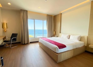Quarto de hotel com uma cama grande, uma cadeira, uma mesa de cabeceira e vista para o mar.
