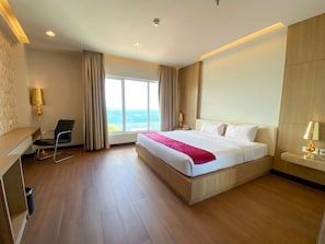 Quarto de hotel com uma cama grande, uma mesa, uma cadeira e vista para o mar.