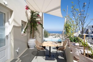 Uma varanda com mesa e cadeiras, um vaso de planta e vista para o mar.