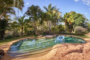 Piscina sinuosa cercada por palmeiras e um caminho de tijolos.