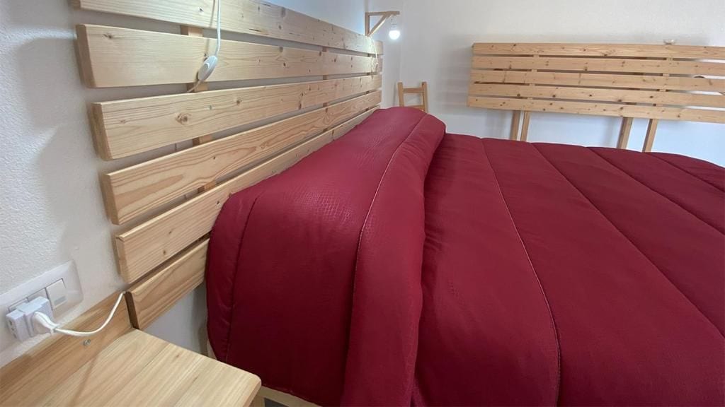 Quarto com cabeceira de madeira, colcha vermelha e mesa de cabeceira.