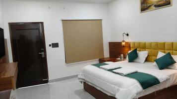 Quarto de hotel com cama, mesa de cabeceira, ventoinha no teto, um quadro na parede e uma porta.