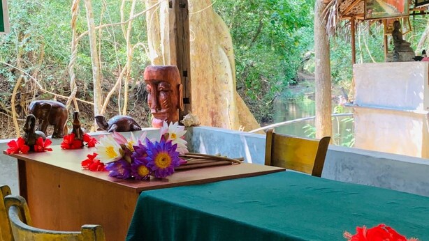 Mesa de madeira com toalha de mesa verde, rodeada por cadeiras e decorada com flores e estátuas.