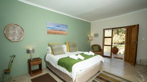 Quarto com cama, mesa de cabeceira, abajur, um brinquedo de girafa, tapete e porta que dá para uma área externa.