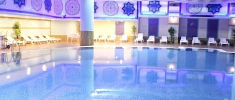 Uma grande piscina interna com espreguiçadeiras e detalhes decorativos nas paredes.