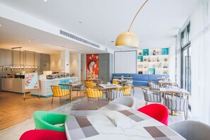 Um saguão moderno de hotel com área de refeições, balcão de recepção e uma grande janela.