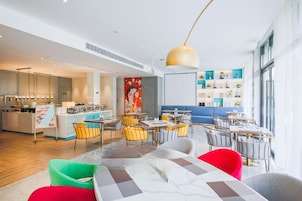 Um saguão moderno de hotel com área de refeições, balcão de recepção e uma grande janela.