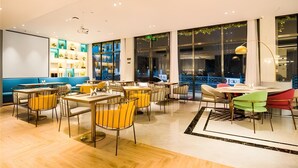 Decoração moderna com diversas áreas de estar, incluindo mesas redondas e cadeiras, e uma grande janela com vista para o exterior.