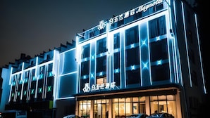 Um hotel com fachada moderna, sinalização iluminada e estacionamento com vários carros.