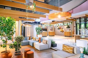 Um saguão de hotel moderno com áreas de estar, balcão de recepção e plantas de interior.