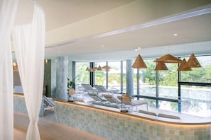 Uma área de spa com balcão de recepção, espreguiçadeiras e amplas janelas com vista para o exterior.