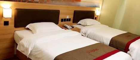 Quarto de hotel com duas camas, cabeceira de madeira, mesa de cabeceira e luminária fixada na parede.