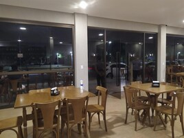 Restaurante com mesas e cadeiras de madeira, amplas janelas e vista para a rua.