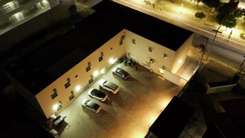 Um estacionamento com vários carros, um prédio com diversas janelas e uma rua ao fundo.
