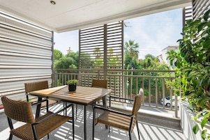 Uma varanda com mesa e cadeiras, um vaso de planta e vista para a rua.