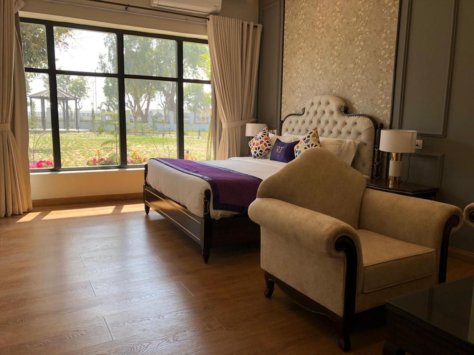 Quarto com cama, cadeira, janela com cortinas e vista para um jardim.