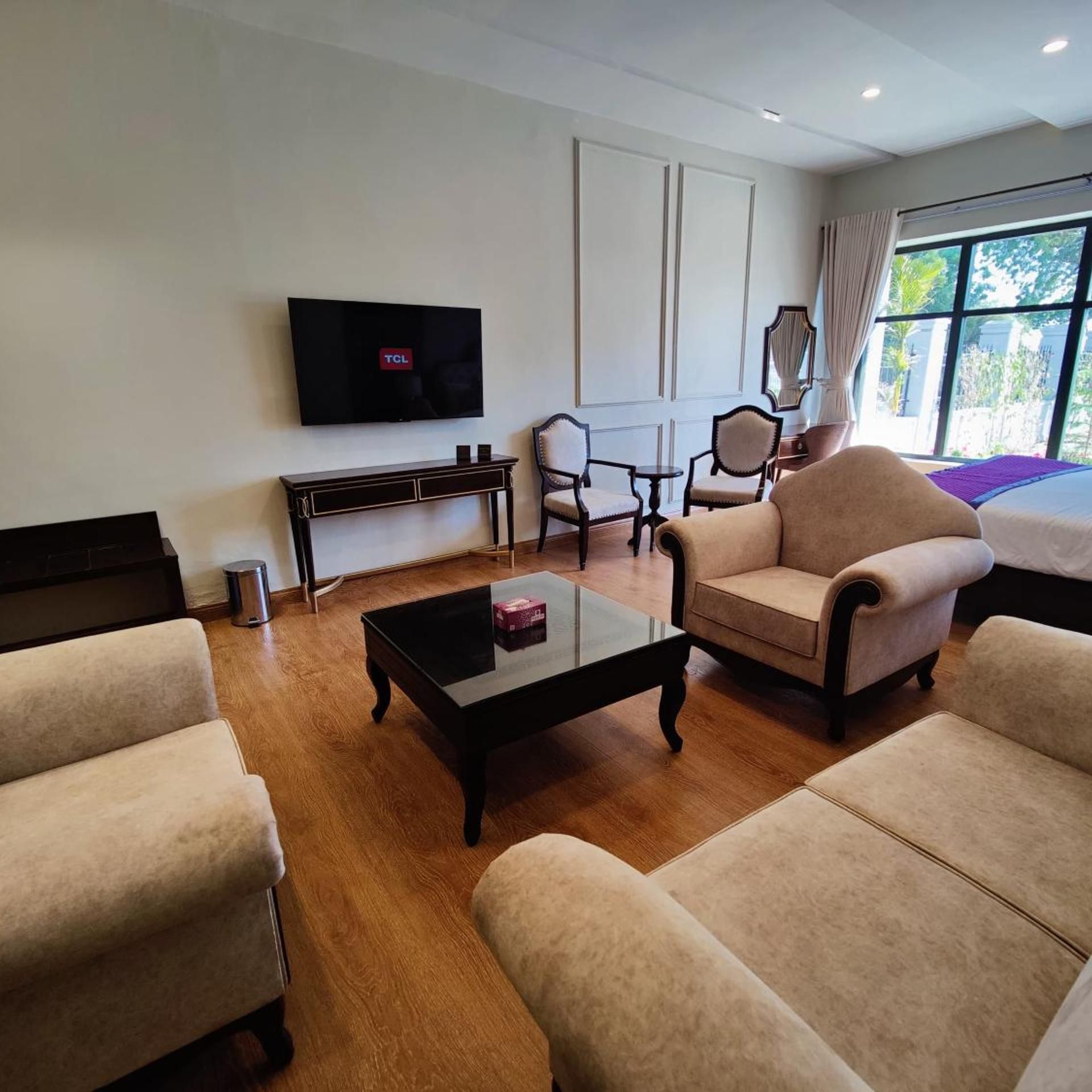 Quarto de hotel com TV de tela plana, sofá, mesa de centro e janela com vista para áreas verdes.
