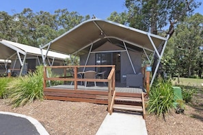 Estrutura moderna em forma de tenda, com deck de madeira e área de estar, cercada por vegetação.
