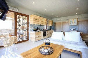 Uma cozinha moderna com armários de madeira e painel de pedra, uma sala de jantar com mesa e cadeiras de madeira, e um quarto com cama grande e roupa de cama branca.