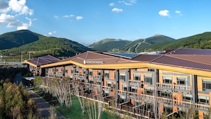 Um hotel moderno com vários edifícios, uma galeria coberta e vista para montanhas ao fundo.