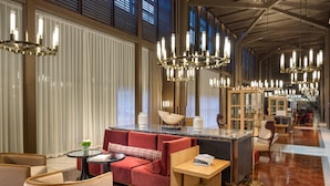 Um hall de hotel espaçoso, com um sofá vermelho, um bar de mármore e várias luminárias de cristal.