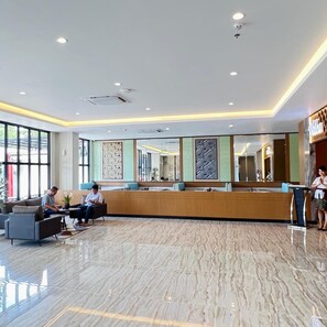 Um hall de hotel com balcão de recepção, área de estar e grandes janelas.