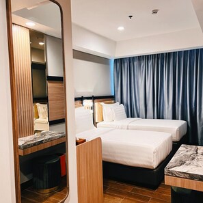 Quarto de hotel com duas camas, um espelho grande, uma mesa com tampo de mármore e uma cortina azul.
