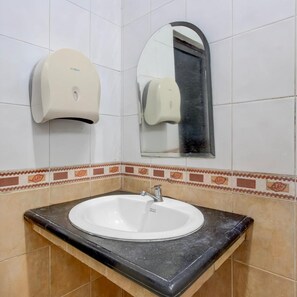 Casa de banho com lavatório branco, espelho e dois dispensadores de sabonete líquido fixados na parede.