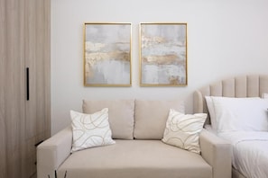 Sofá em tons neutros com almofadas estampadas, guarda-roupa de madeira e duas pinturas abstratas na parede.