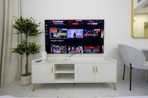 Televisão de tela plana presa em um armário branco com puxadores dourados, exibindo diversos conteúdos de streaming.