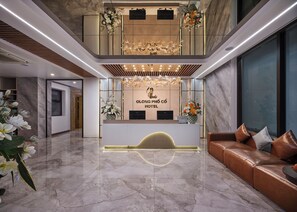 Uma área de recepção de hotel com design moderno, com balcão de atendimento, espaço para sentar e arranjos florais decorativos.