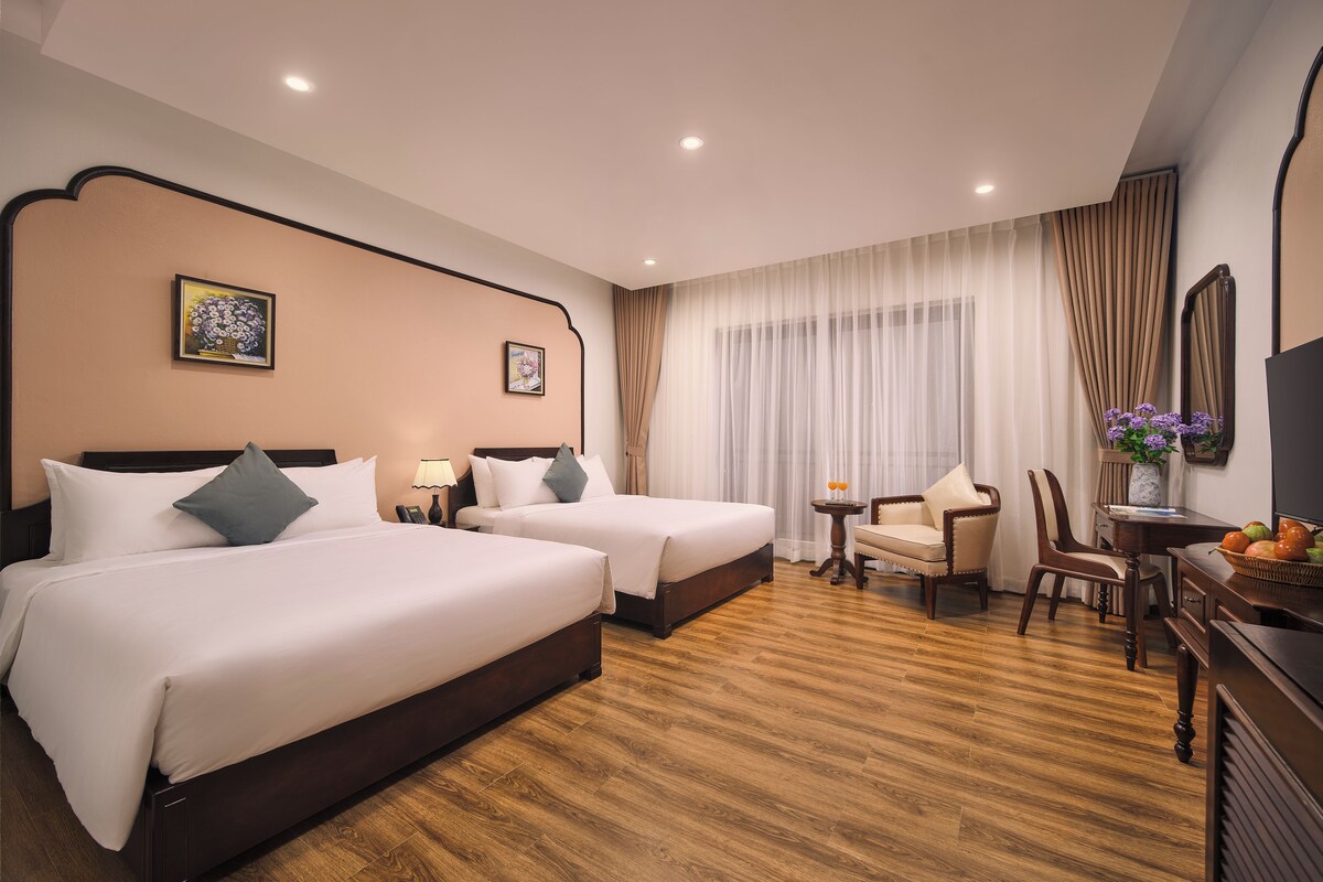 Quarto de hotel com duas camas, uma escrivaninha, uma cadeira, televisão e uma janela com cortinas.