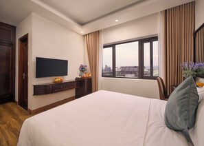 Quarto de hotel com cama, televisão de tela plana, janela com cortinas e vista para edifícios.