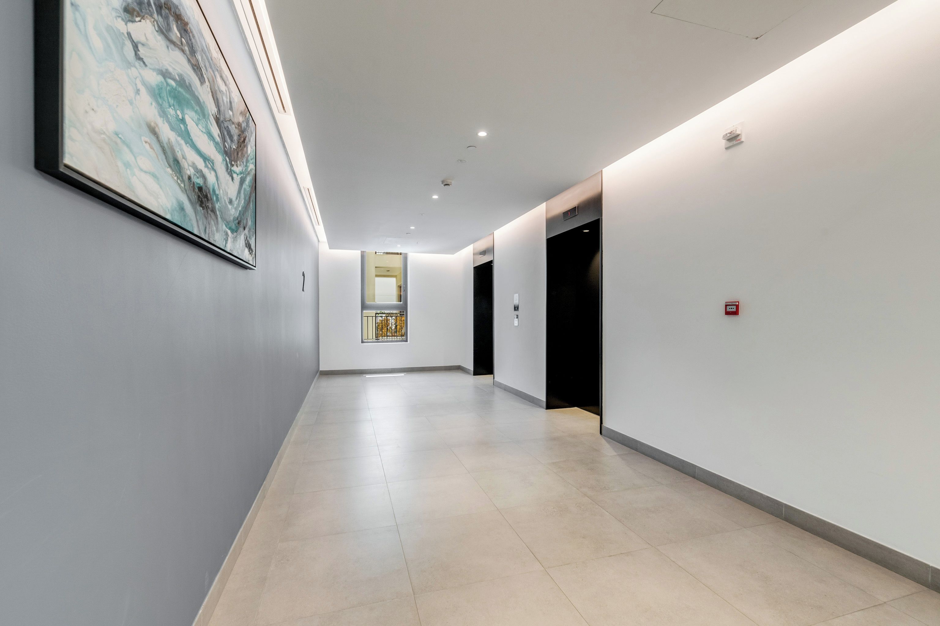 Corredor com uma grande pintura abstrata à esquerda, uma janela com vista para árvores e duas portas à direita.