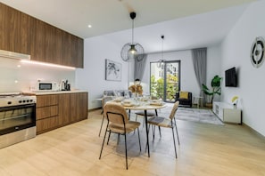 Cozinha moderna com eletrodomésticos embutidos, sala de jantar com mesa e cadeiras redondas, e sala de estar com sofá e televisão.