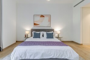 Quarto moderno com uma cama grande, duas mesas de cabeceira com abajures, uma cabeceira e uma pintura abstrata na parede.