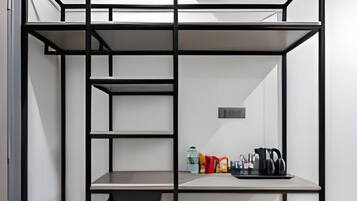 Quarto moderno e minimalista com mesa embutida, estantes e pequena área de cozinha.