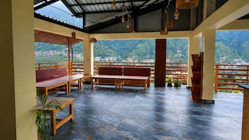 Varanda espaçosa com vista para uma paisagem montanhosa, mobiliário de madeira e luminárias pendentes.