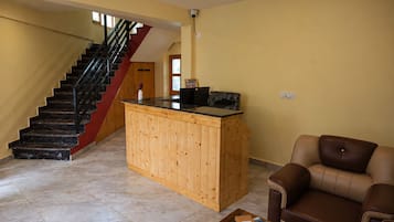 Sala de estar com um balcão de madeira, sofá de couro marrom e escada com detalhes vermelhos.