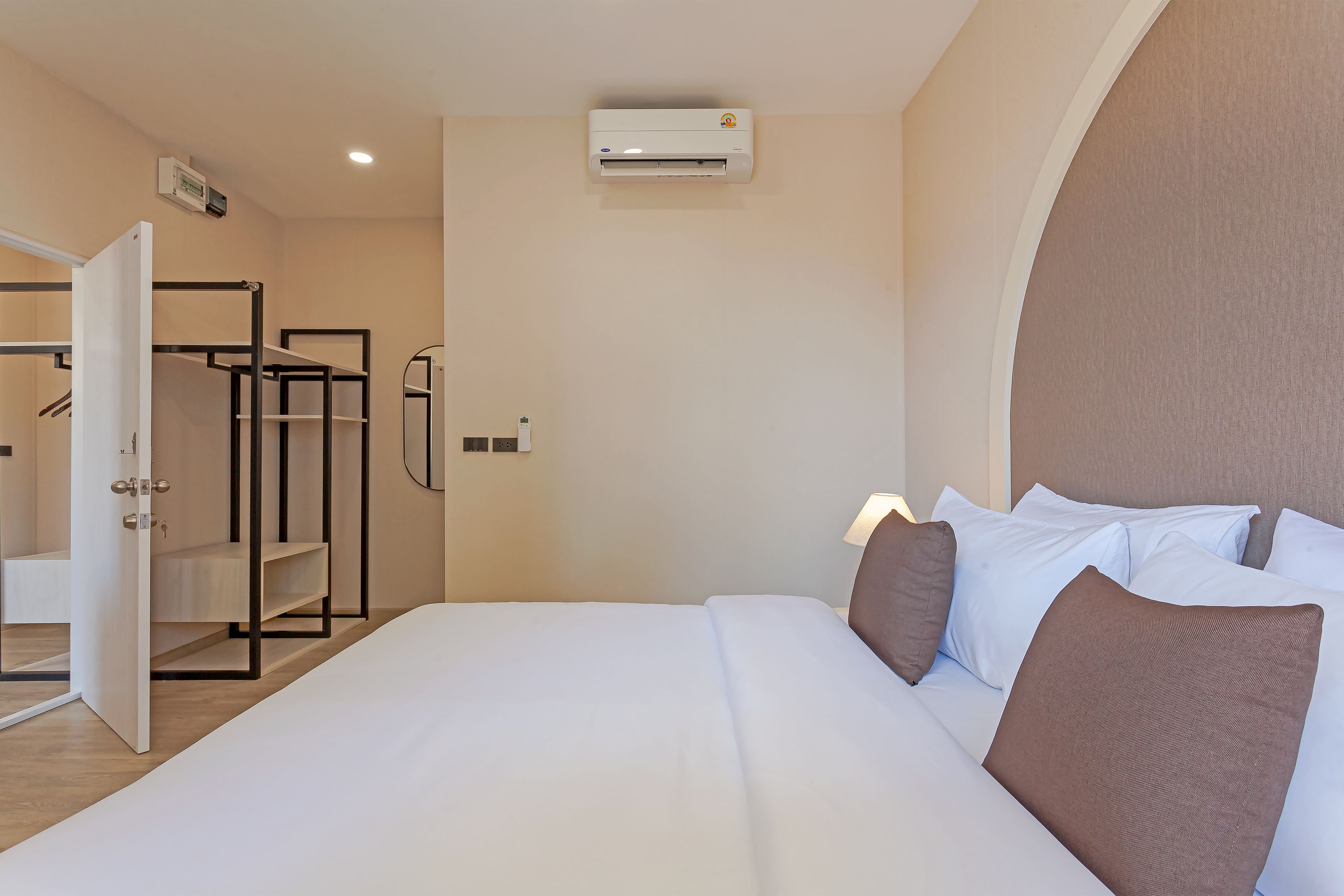 Quarto de hotel com cama, guarda-roupa, espelho, ar condicionado e porta para o banheiro.