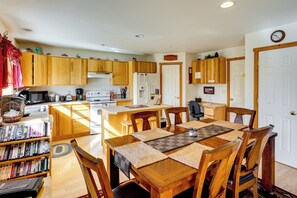 Cozinha compacta com armários de madeira, uma mesa de jantar com cadeiras e uma estante repleta de livros.