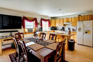 Cozinha compacta com armários de madeira, uma mesa de jantar com jogos americanos e uma TV de tela plana.