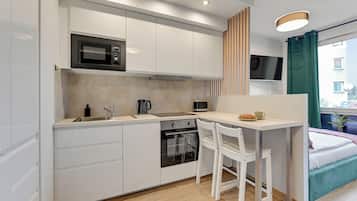 Uma cozinha compacta com armários brancos, micro-ondas, forno e uma pequena área de refeições com uma cadeira branca.