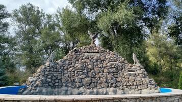 Uma fonte de pedra com duas estátuas de lobo, rodeada por árvores.