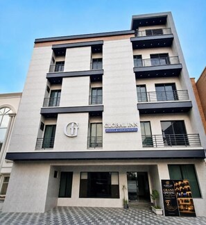 Hotel de vários andares com fachada moderna, logotipo em destaque e placa indicando que oferece quartos de hotel e apartamentos.