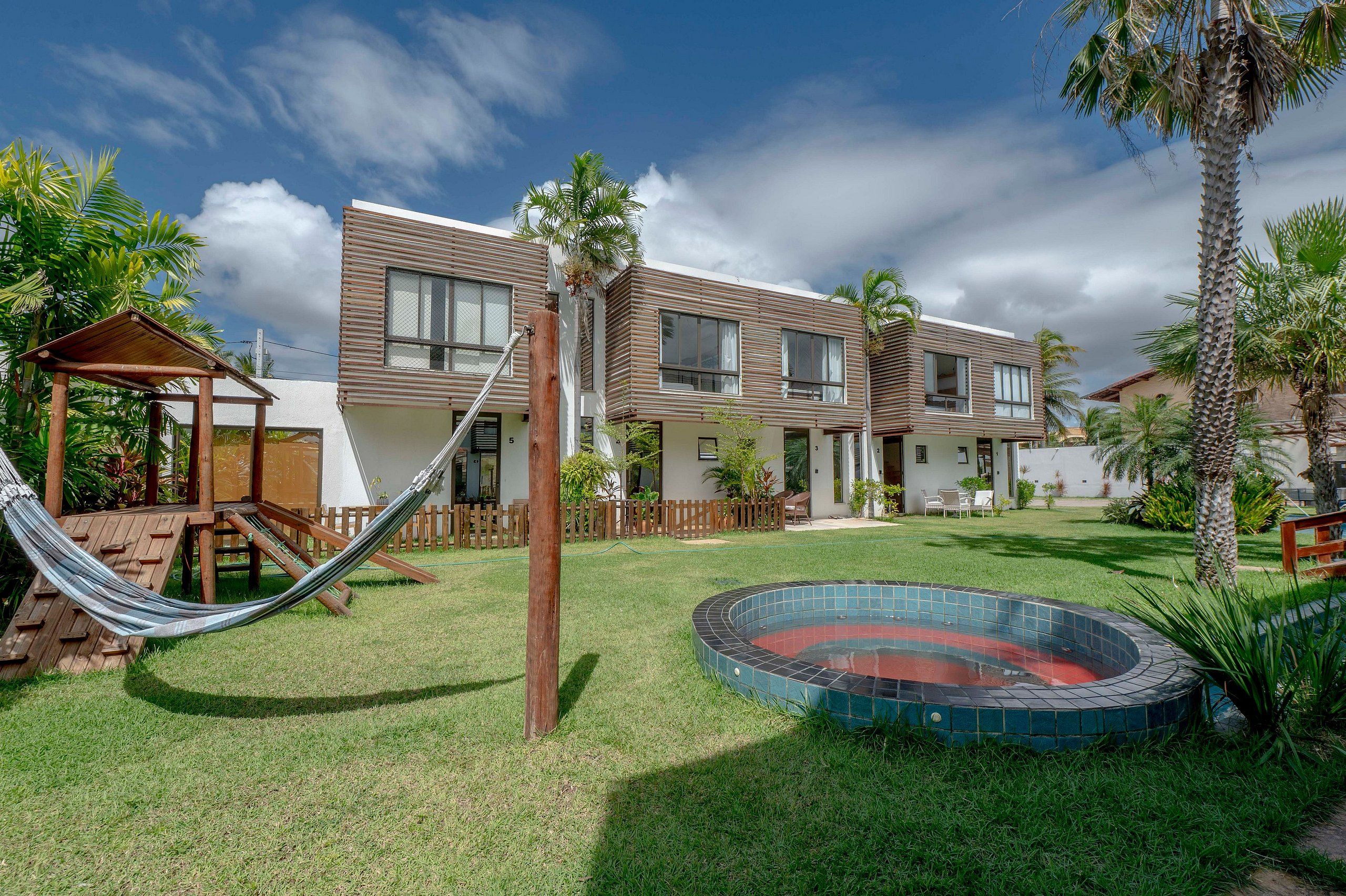 Uma casa moderna com dois andares, piscina, rede e deck de madeira.