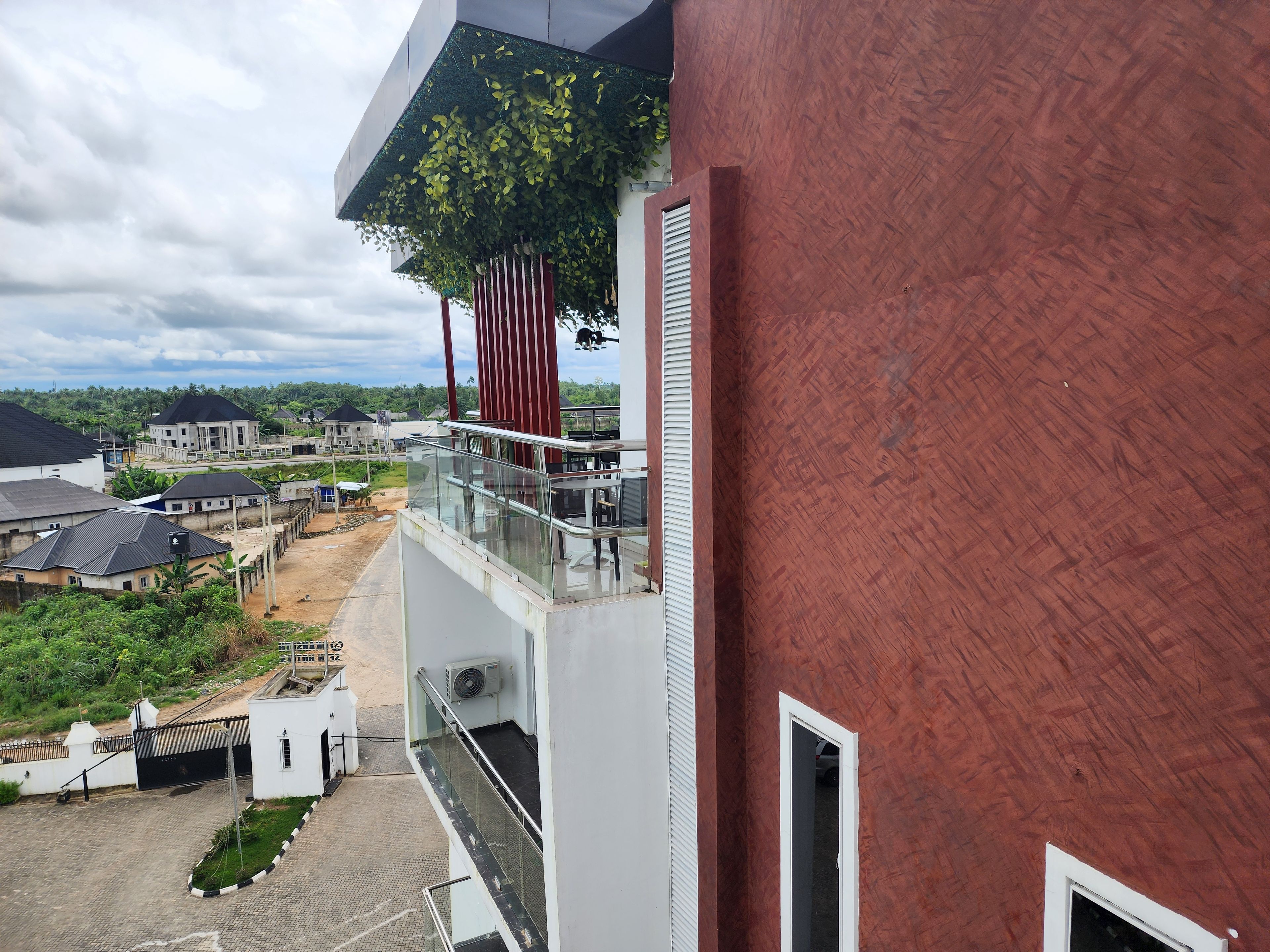 Um edifício de vários andares com varanda, fachada vermelha e vista para uma área de construção ao fundo.